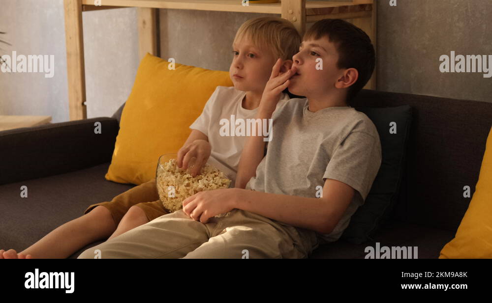 Two little boys eat popcorn sitting on the couch and watching TV. close ...