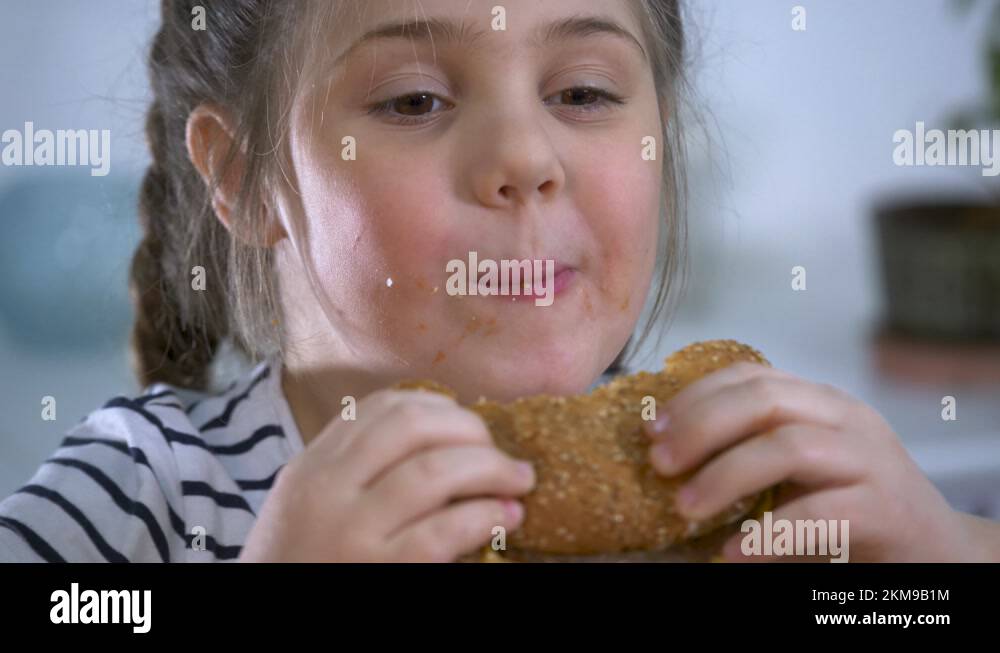 Little girl in fast food cafe eats burger. Portrait of hungry child ...