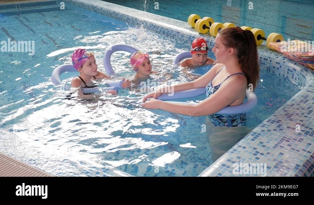 A swimming coach teaches a group of children to swim and dive in an ...