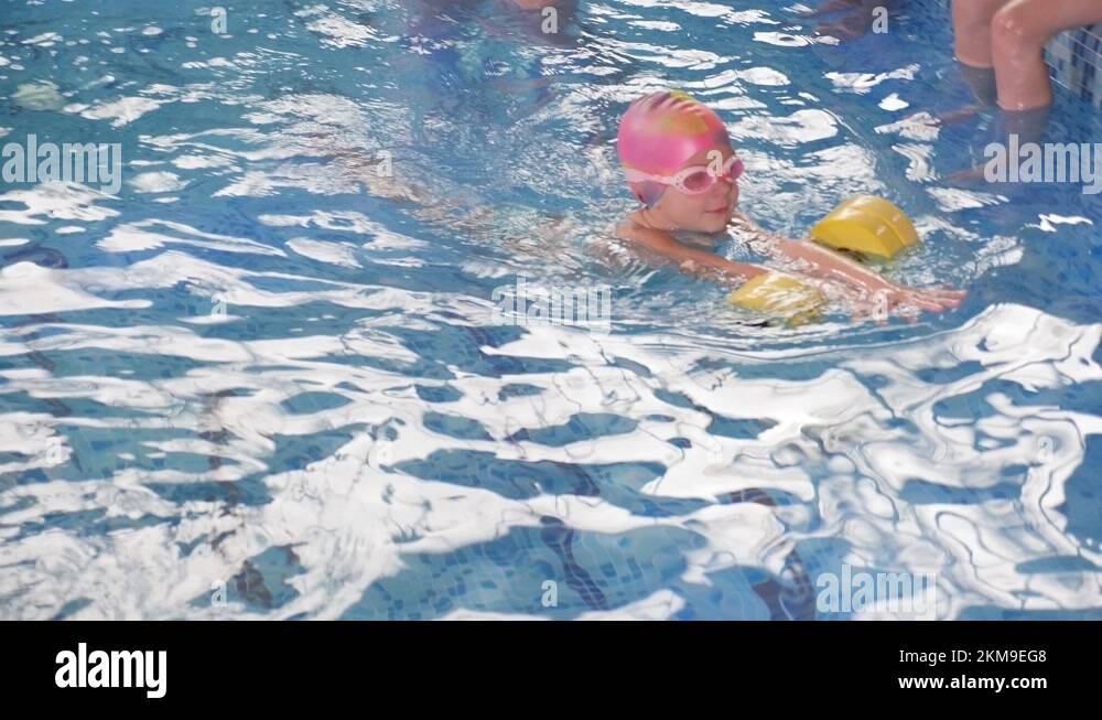 A little girl learns to swim in the pool and swims with a foam dumbbell ...