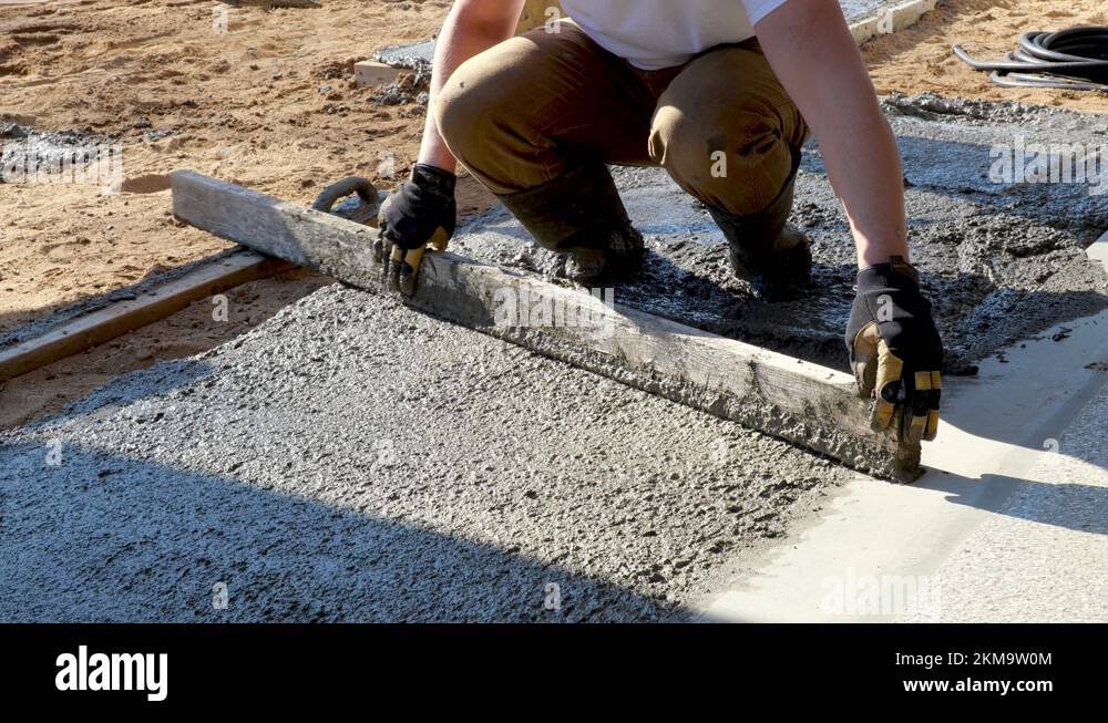 A 2 x 4 board is used as a screed to level wet cement of new garage ...