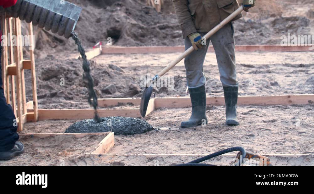 Lots of wet fresh cement is pouring, construction worker is shoveling ...