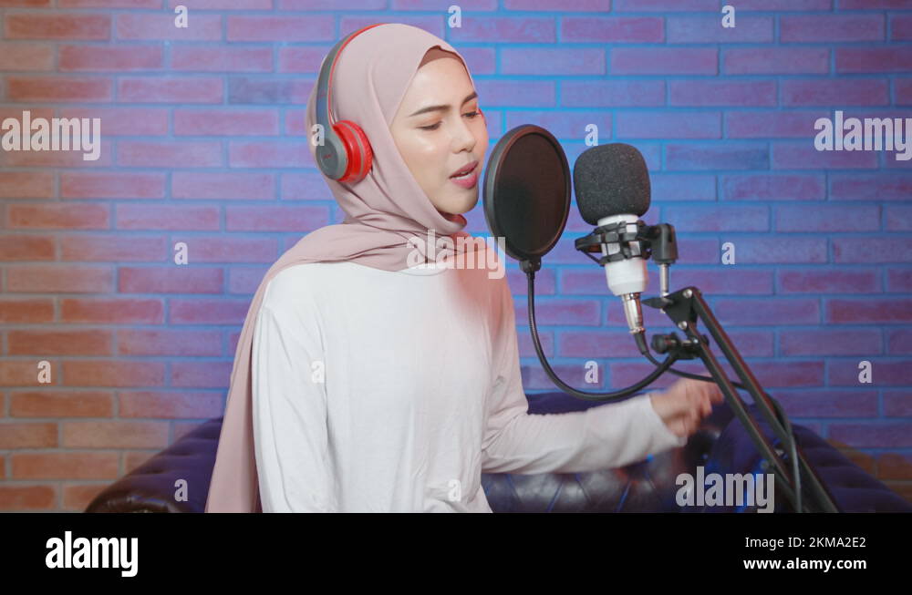 Young smiling muslim female singer wearing headphones with a microphone ...