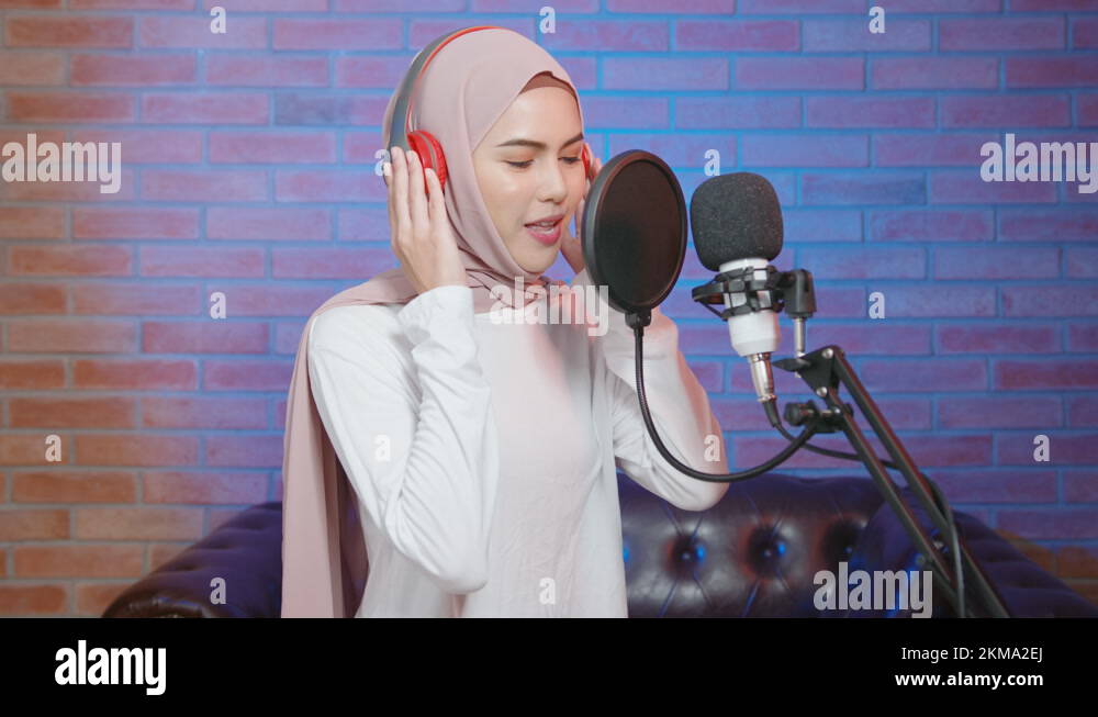 Young smiling muslim female singer wearing headphones with a microphone ...