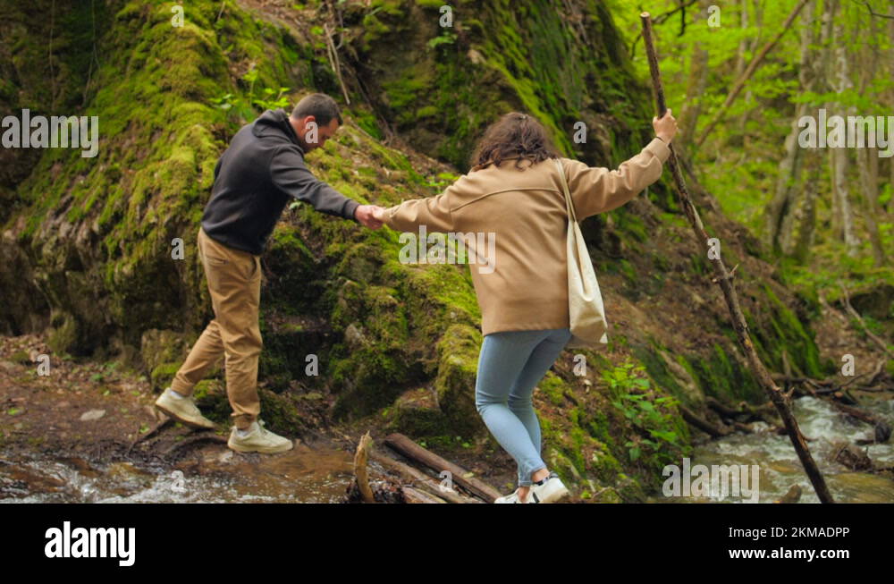 Young man helping woman across makeshift bridge whilst walking in the ...