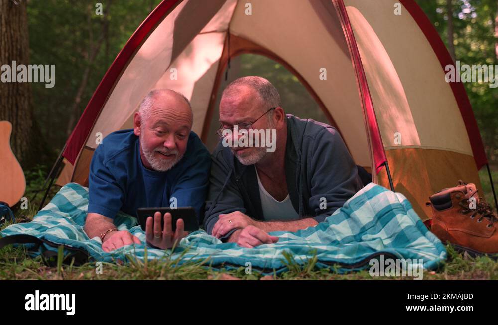 Two gay men with pride flag and tent in front of campfire talking to ...