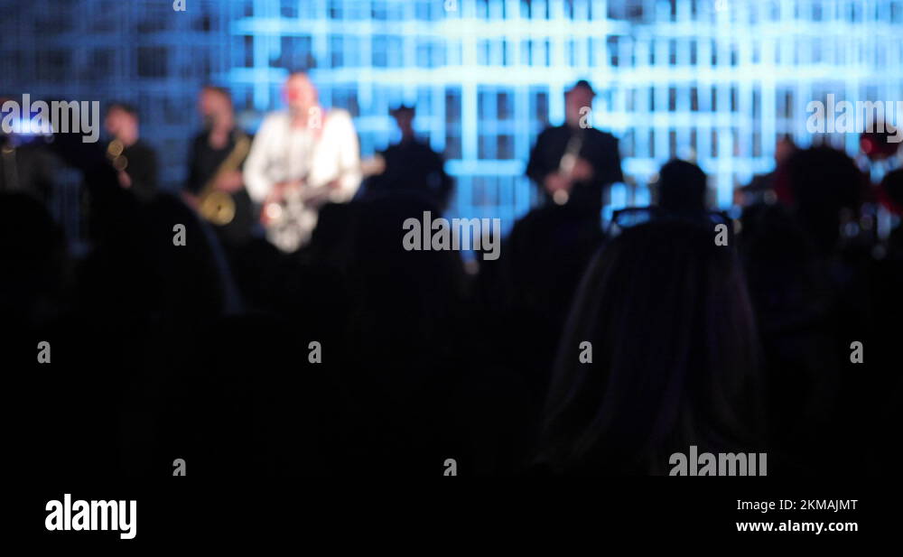 Musical band performing on bright scene in front of fans crowd at night ...