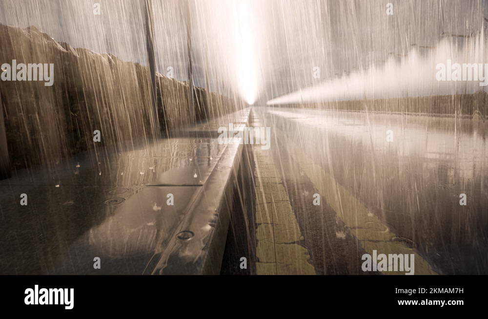 Raindrops bouncing off the surface of a rain-soaked sidewalk and road ...
