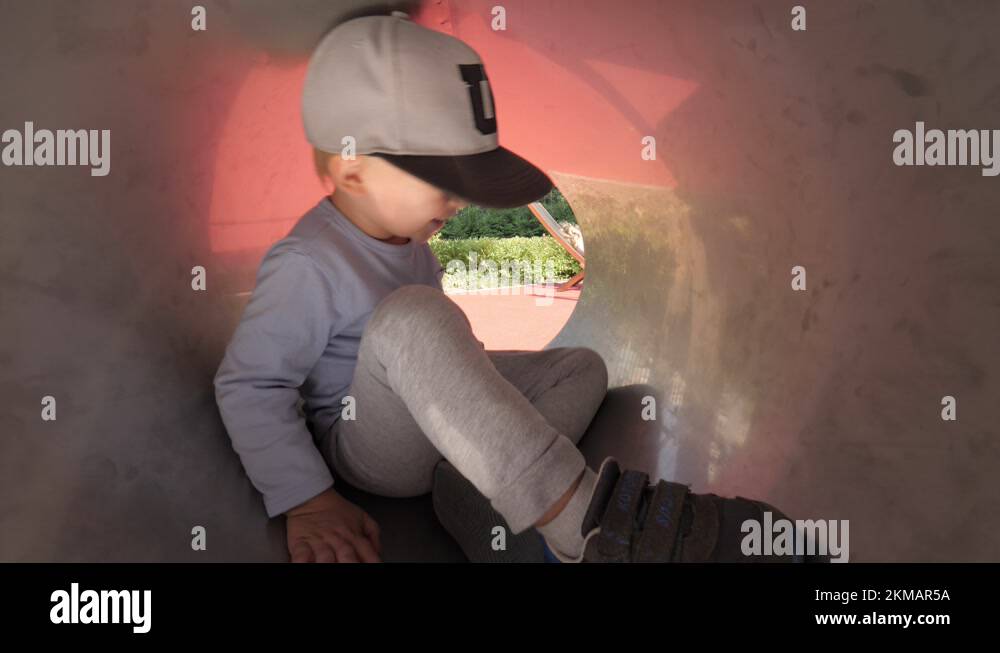 Funny little boy playing in pipe slide attraction at child playground ...