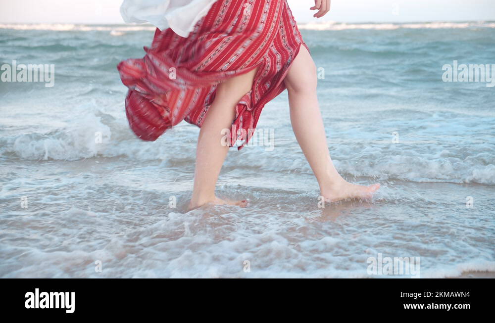 Woman legs wearing long dress walking on the beach in shallow water ...