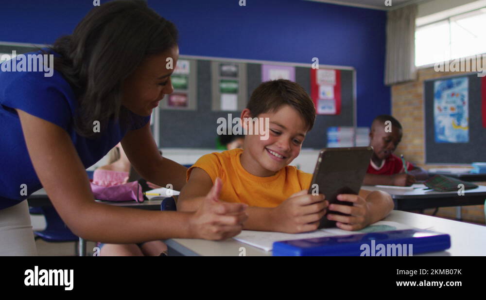 Diverse smiling female teacher helping schoolboy sitting in classroom ...