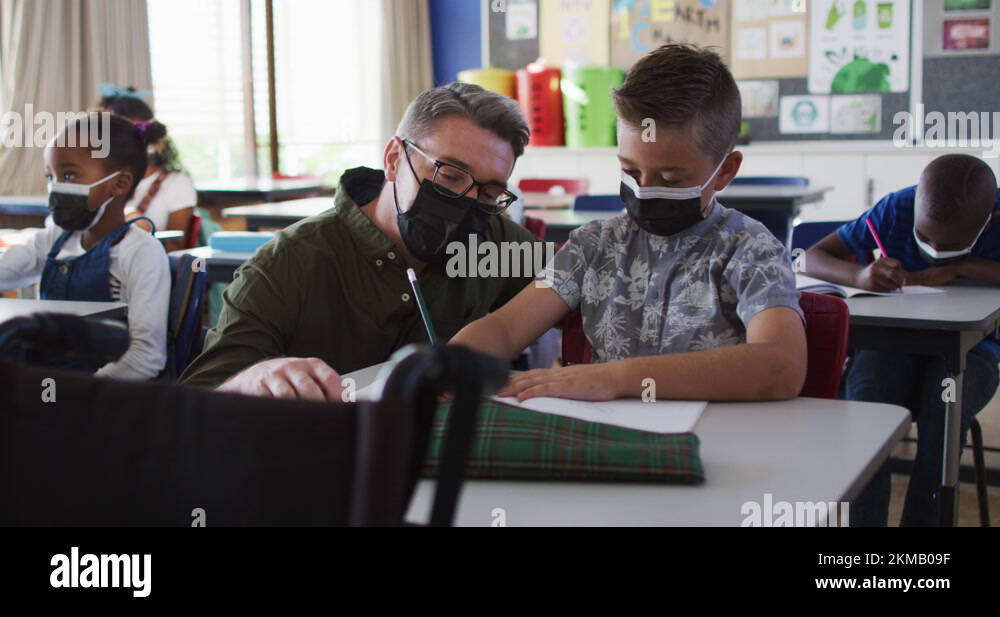 Diverse male teacher helping schoolboy sitting in classroom, all ...