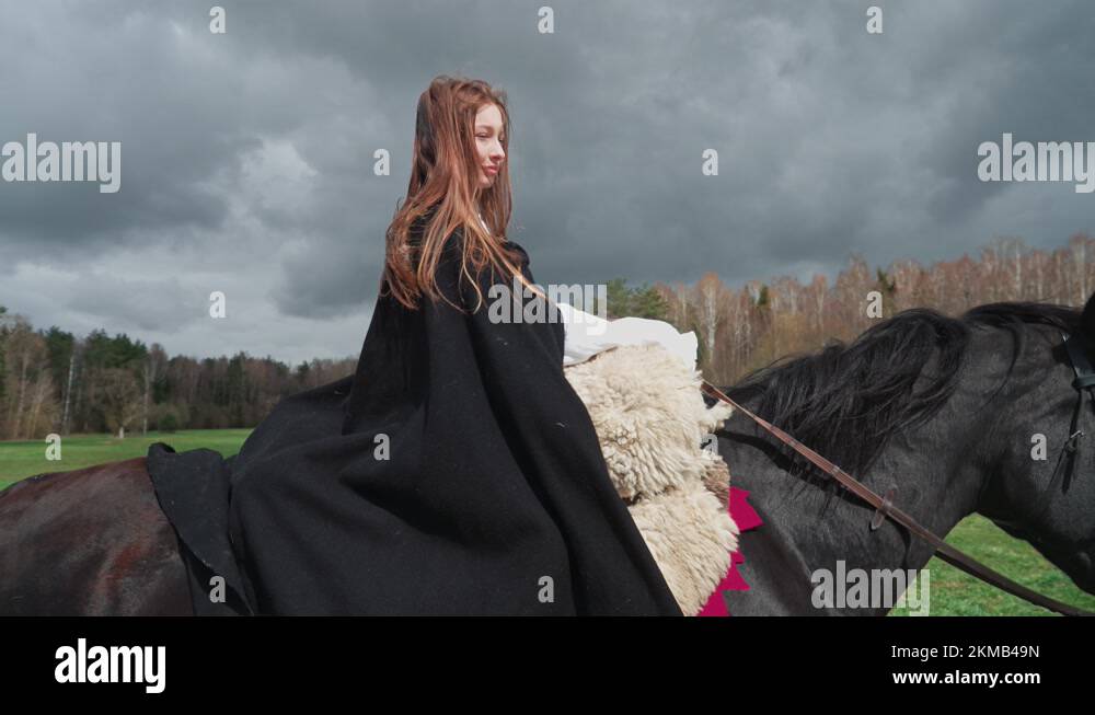 Beautiful female in a medieval dress riding a horse through a ...