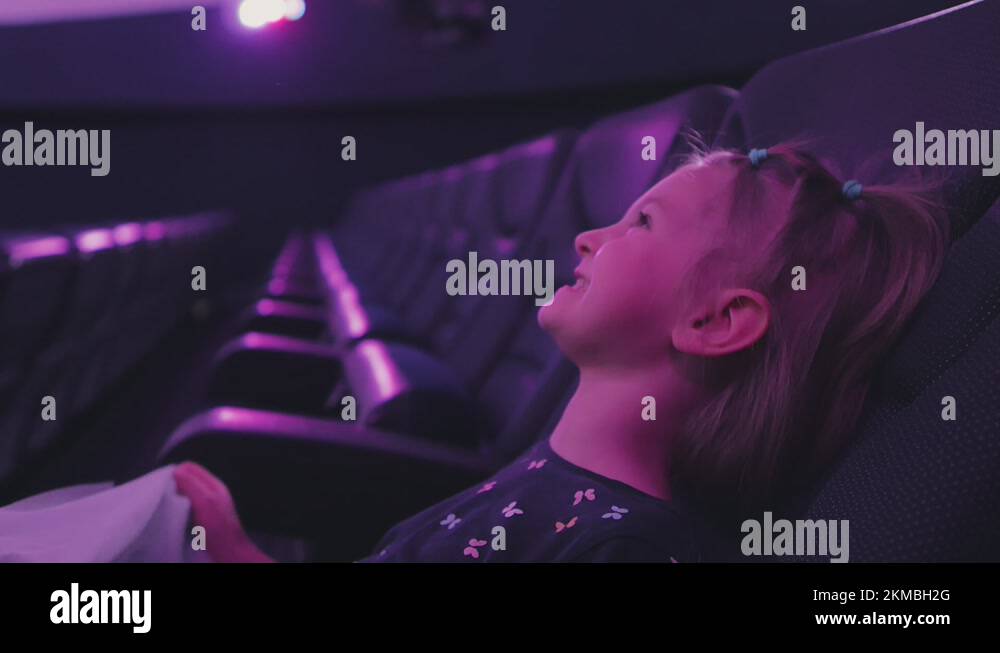 A little girl sitting in the planetarium auditorium looks up and laughs ...