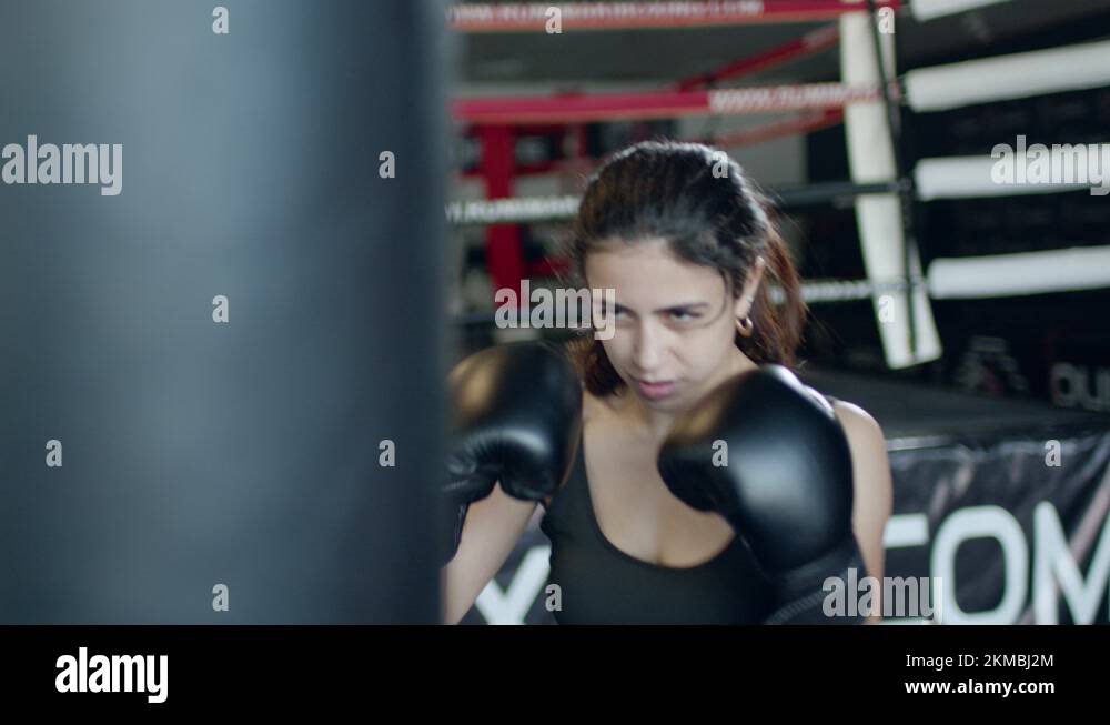Boxing, woman fighter trains her punches, beats a punching bag ...