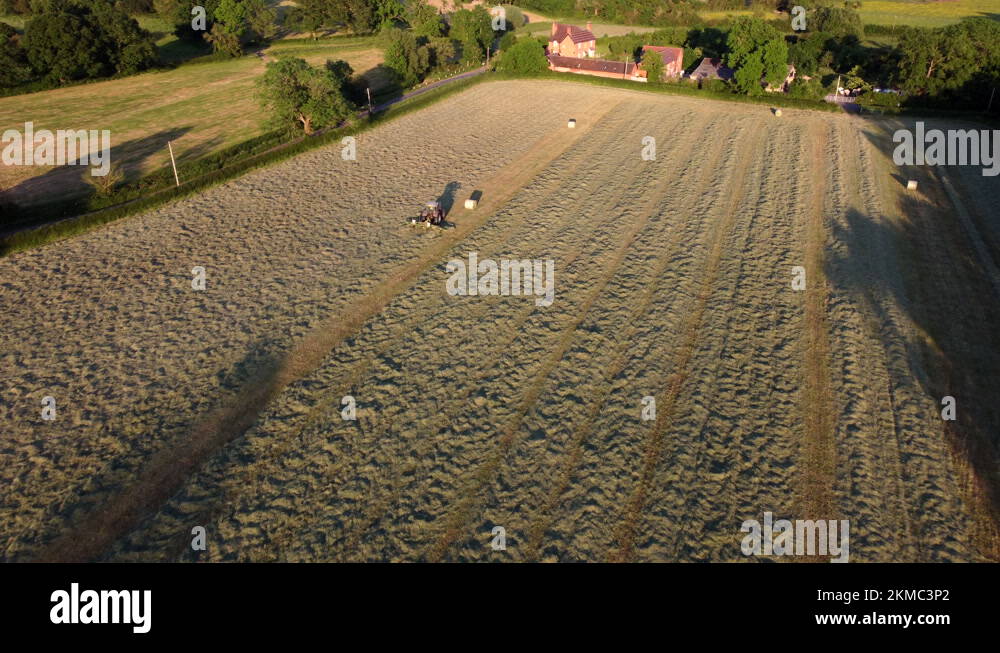 Long evening shadows are cast over the land as a tractor works in a ...