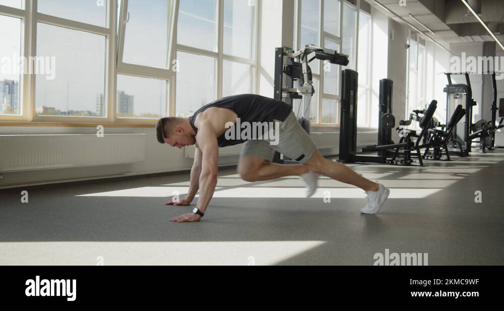 Young muscular athlete works out in modern gym making mountain climbers ...