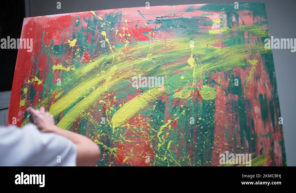 Back view, female artist draws with spray, paint on a large canvas in a ...