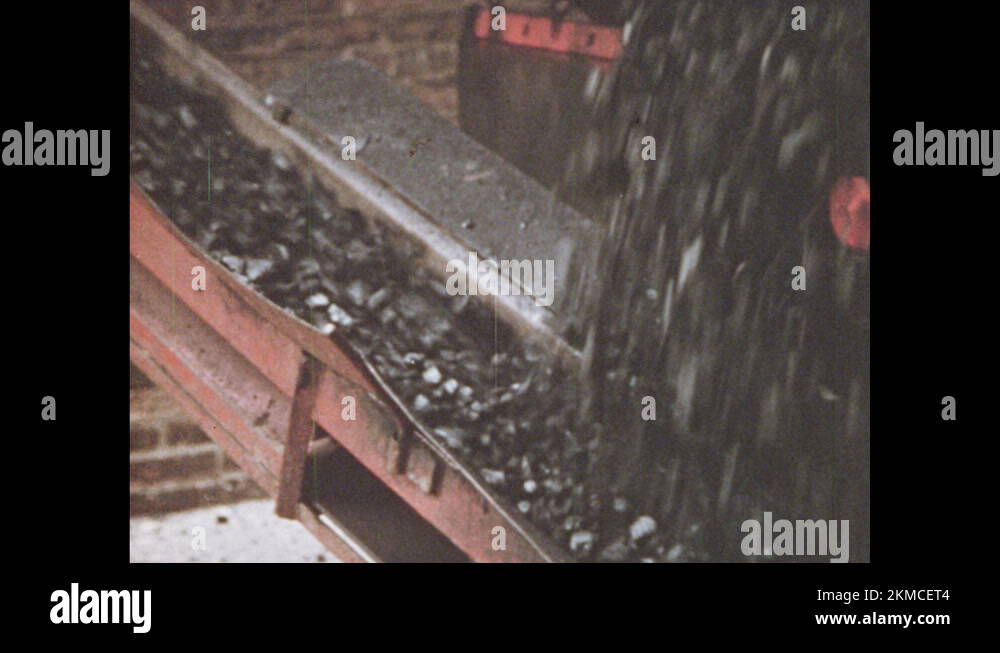 1970s: Coal cascades from truck into troughs. Family walks by fenced ...