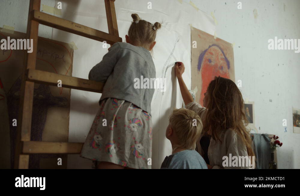 Back view of female painter and children painting on wall with black ...