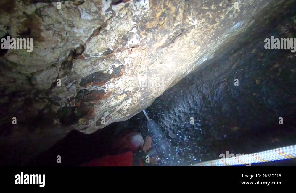 Person drilling a hole in a cave with electrical drill hanging by a ...
