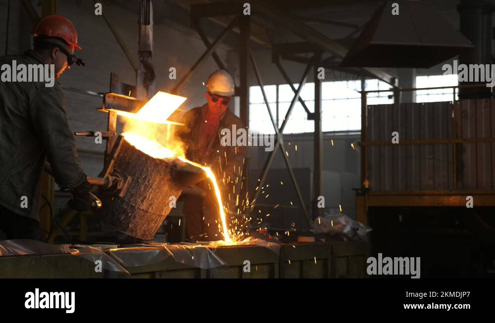 Two men bending a metallic barrel with bright orange iron falling in ...