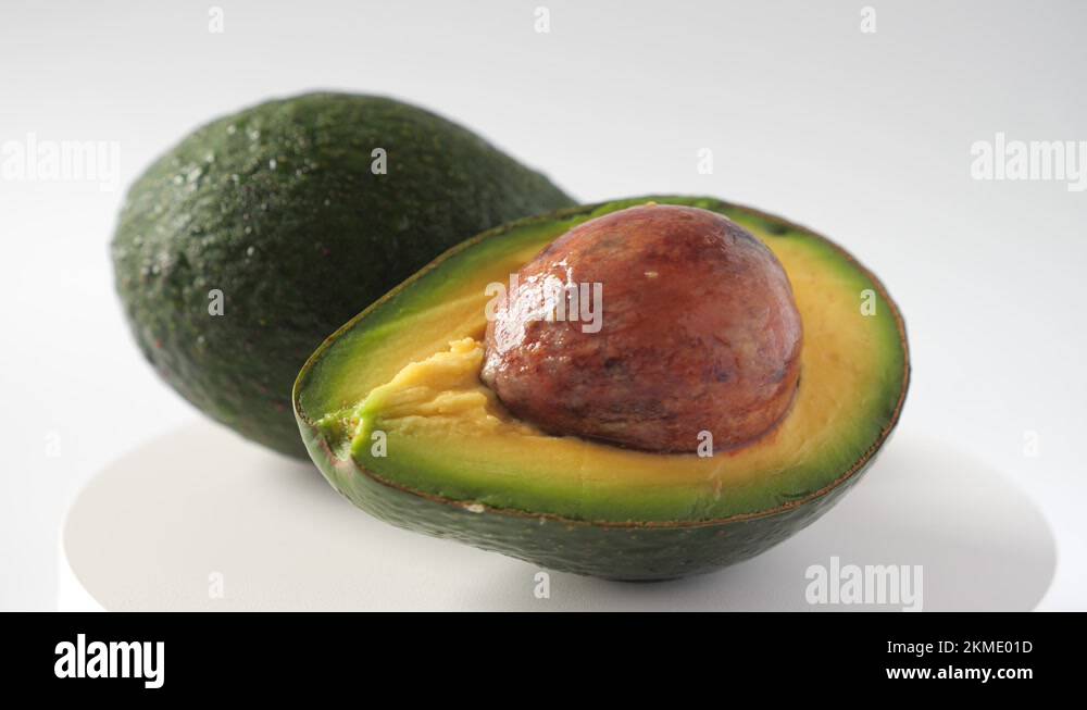 Whole and cut in half fresh Avocado fruit turning on white background ...