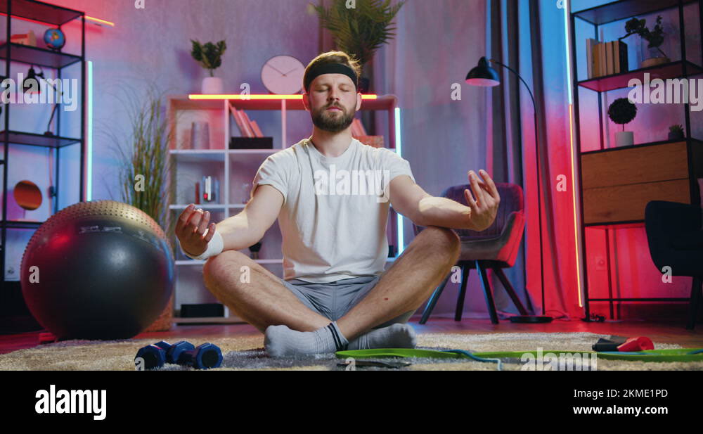 Handsome relaxed young bearded guy in sportswear sitting in lotus pose ...