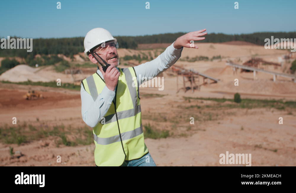 Handheld handsome sand quarry foreman instructing workers using walkie ...