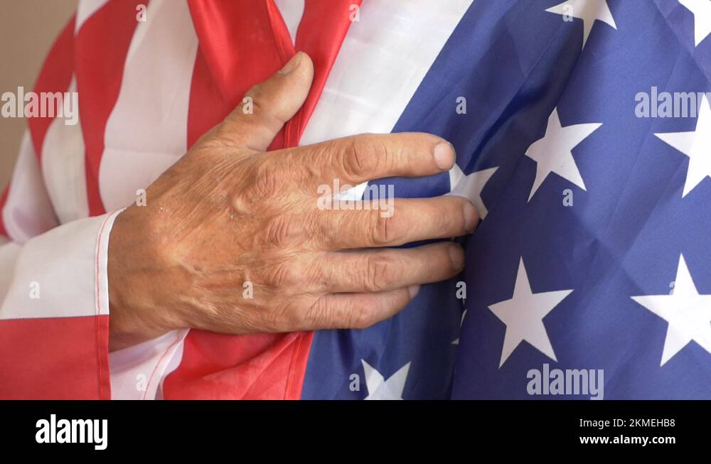 An elderly man sings the national anthem wrapped in a flag with his ...