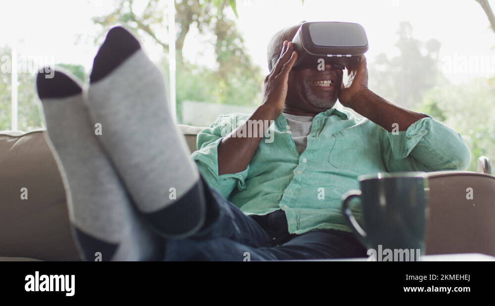 Happy african american senior man sitting with feet up using vr headset ...