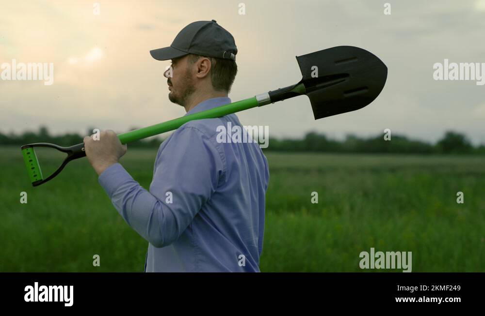 Farming concept. A farmer with shovel in his hands walks across field ...