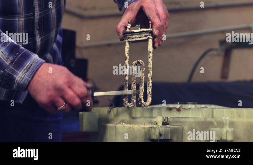 The hands of the master remove the old heating element from the drum ...