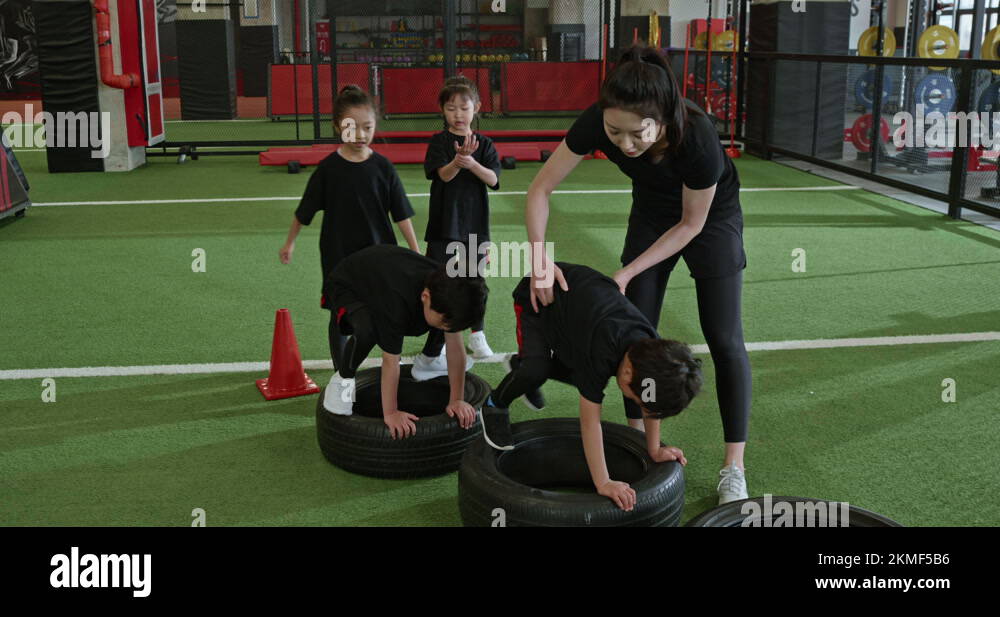 Active Chinese children having exercise class with their coach in gym ...