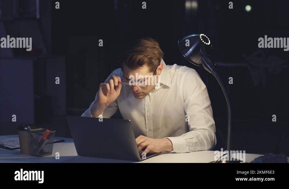 A tired man is looking at a financial report on a computer in the ...