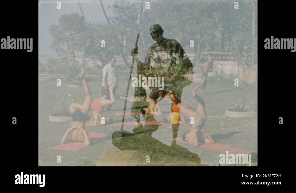 1970s: Statue of Gandhi. Group of men in park practicing asana yoga ...