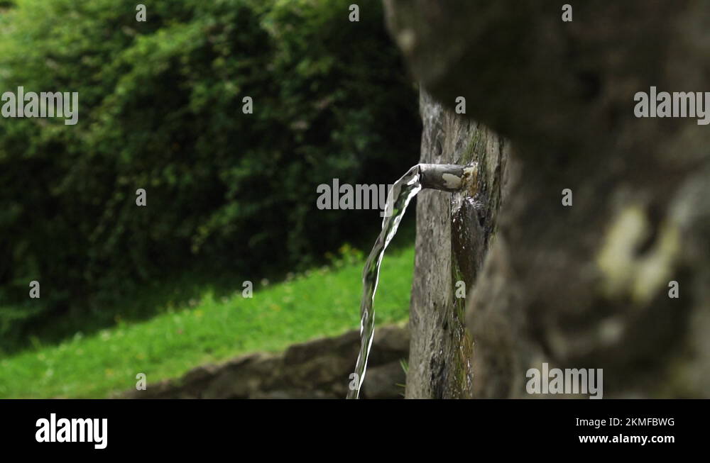 The water of a mineral mountain spring with an ancient stone wall pours ...