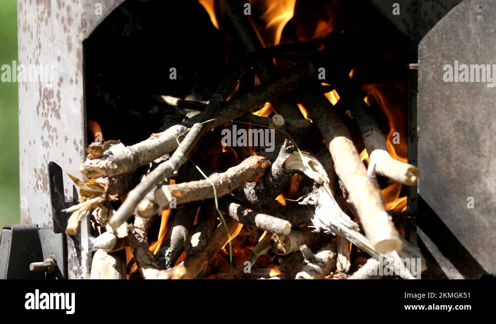 Fire burns in a metal stove for hiking. Charred branches smolder in the ...