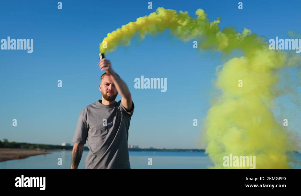 Man spins yellow smoke signal bomb with smoke bomb on beach. Young guy ...