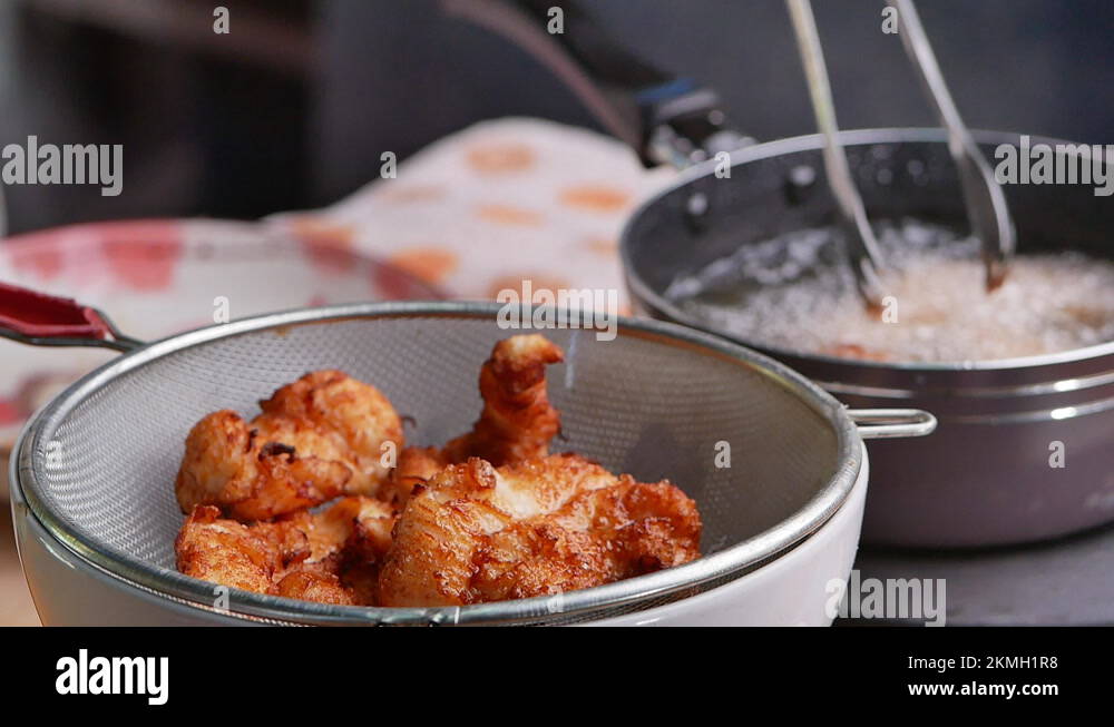 Hands of a woman in gloves is frying marinated chicken in hot oil in a ...