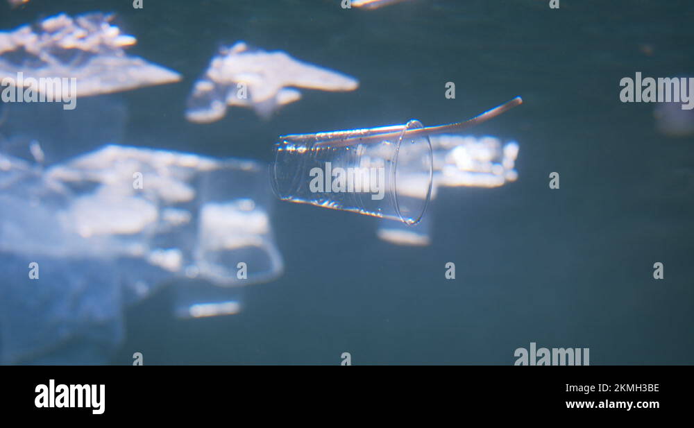 Cinematic close-up on discarded single use cup with straw floating ...