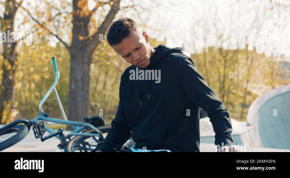 A cyclist who has fallen off bike, a bmx, and is sitting on a concrete ...