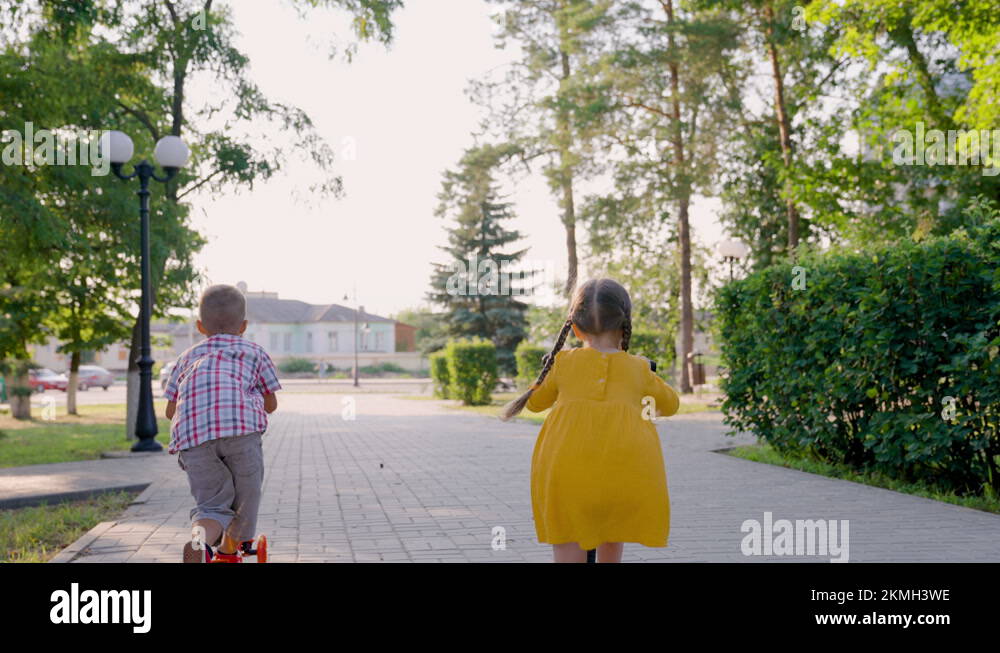 Girl and boy ride scooter together outdoors. Happy cute kids playing in ...