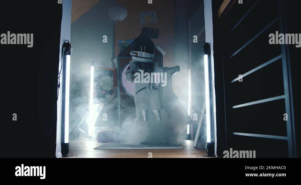 Cinematic zoom in on fun astronaut child dancing in space suit in dark ...