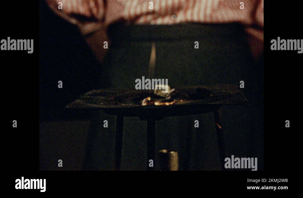 1950s: Objects on grate over fire, objects burning. Boy sitting outside ...