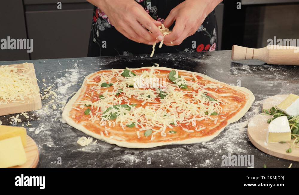 Female chef adding cheese on pizza base, preparing italian pizza ...