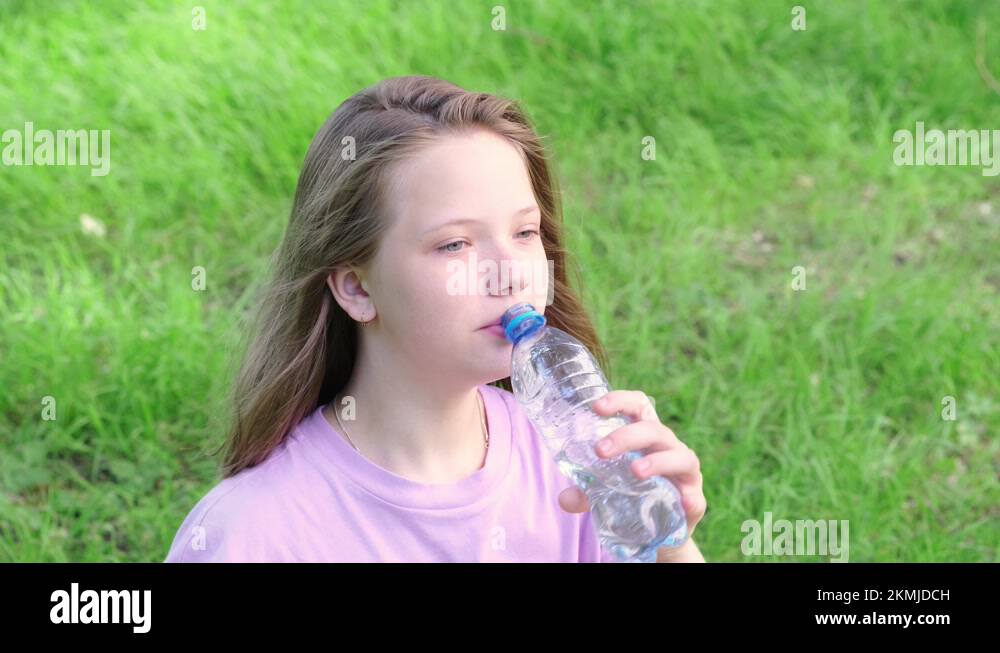 Girl drinks clean drinking water from a bottle in a green city park on a hot Stock Video Footage ...