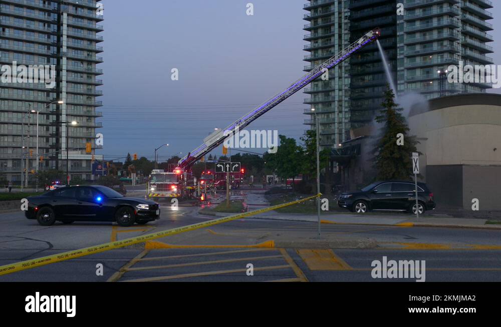 Fire engine and high raised ladders extinguishing fire, yellow taped ...