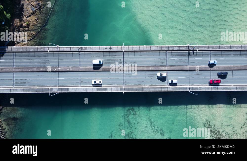Busy coastal road and pedestrian bridge spanning a clear ocean estuary ...