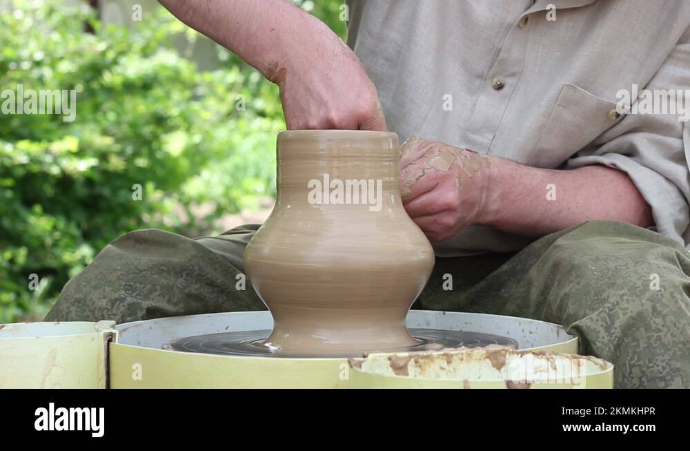 a Caucasian male potter sculpts a large, tall clay pot on a spinning ...
